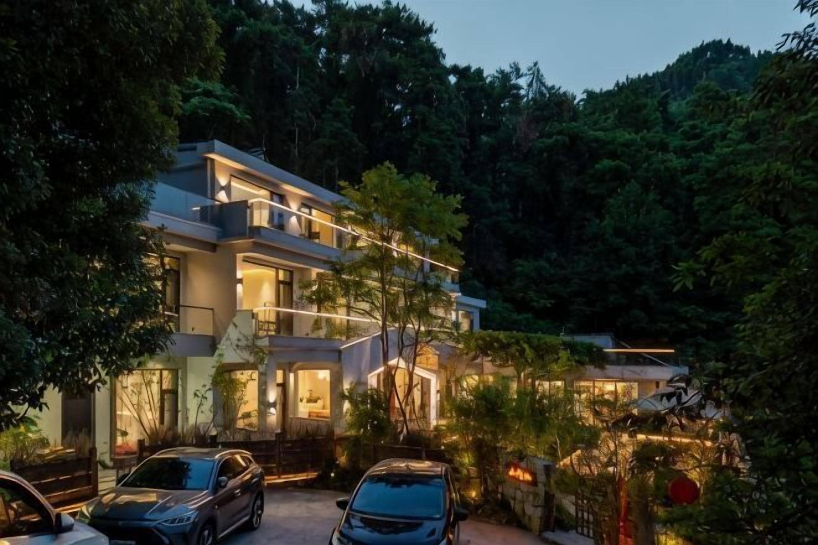 Uma casa moderna de vários andares com entrada por uma calçada, cercada por árvores.