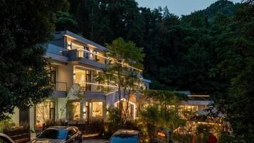 Uma casa moderna de vários andares com entrada por uma calçada, cercada por árvores.