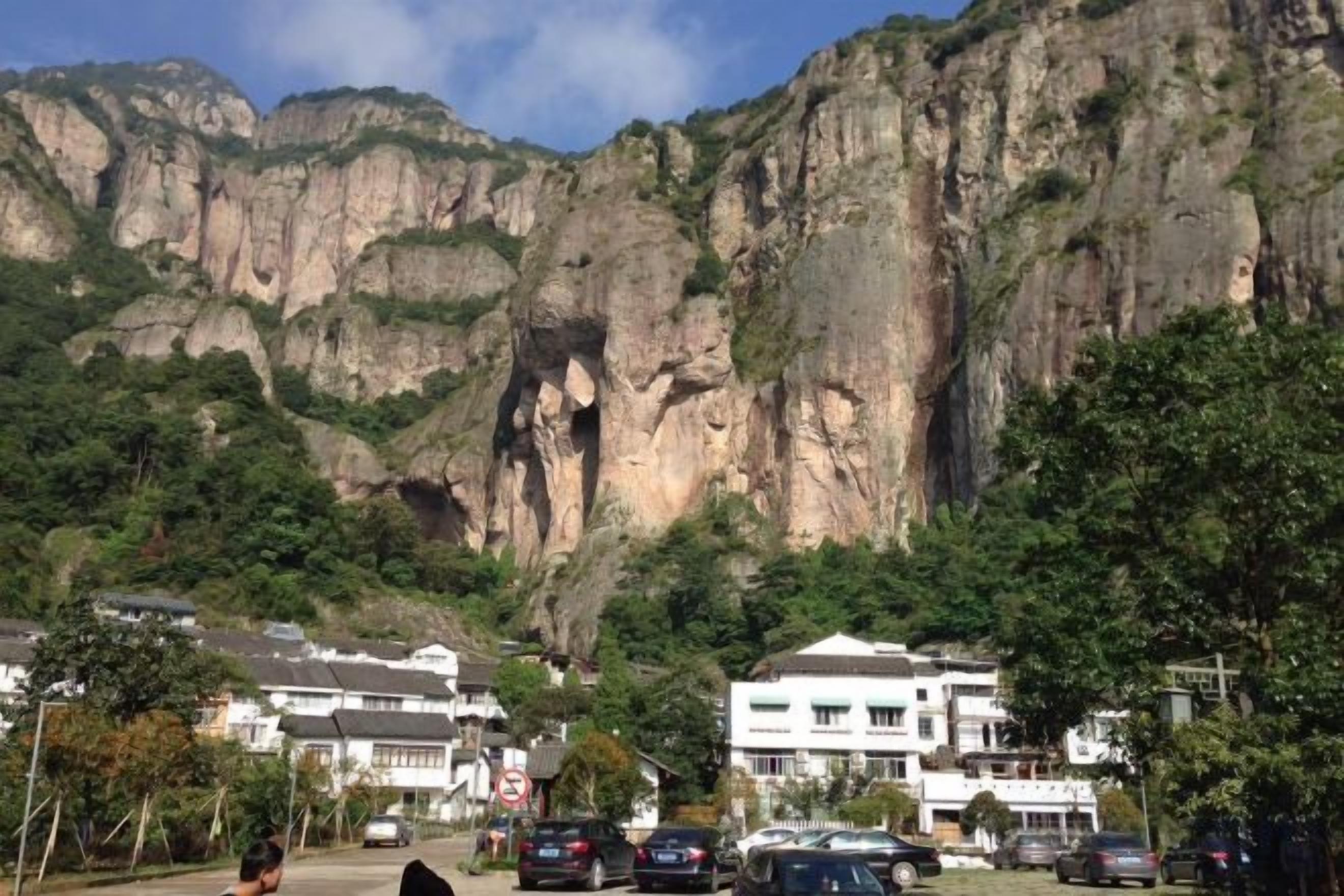 Edifício com montanhas ao fundo, área de estacionamento e céu claro.