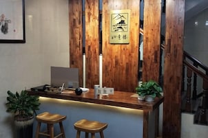 Bancada de recepção com um laptop, uma planta em vaso e uma placa indicando um restaurante.