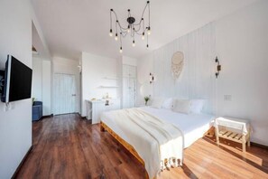 Quarto com uma cama grande, piso de madeira, televisão e lustre.