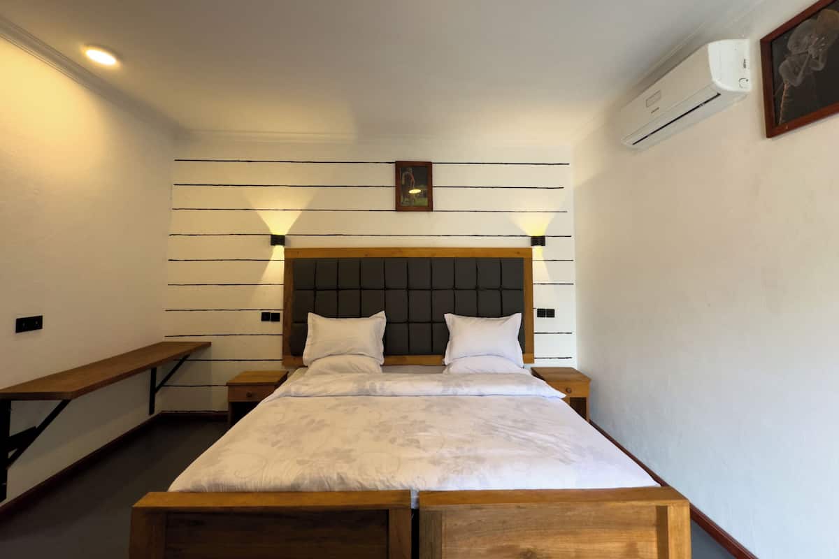 Quarto com cama de madeira, duas mesas de cabeceira, um banco, ar condicionado fixado na parede e um porta-retrato.