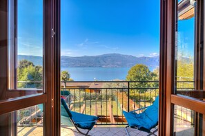 Uma varanda com duas cadeiras azuis, vista para um lago e montanhas ao longe.