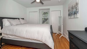 Quarto com cama, ventoinha no teto, cômoda e porta que dá para outro espaço.