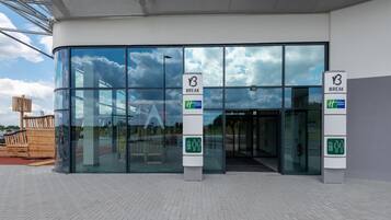 Entrada moderna de um edifício com portas de vidro, logotipo Holiday Inn Express e uma placa indicando uma área de descanso.