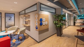 Um espaço de escritório moderno com balcão de recepção, área de estar e placas indicativas para serviços como 'Co-Working' e 'Hotel'.