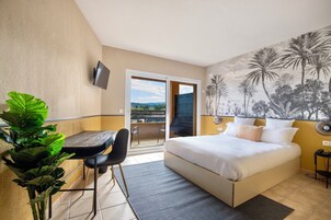 Quarto de hotel com uma cama, uma escrivaninha, uma cadeira, uma televisão, varanda com vista e um mural na parede.