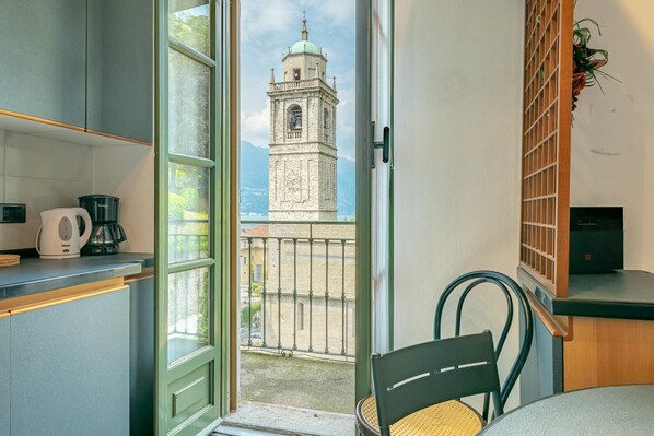 Uma varanda com vista para uma torre, uma cadeira, uma mesa e uma cafeteira.