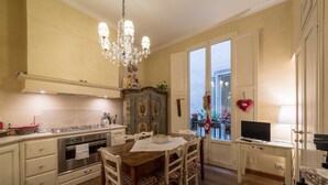 Uma cozinha com uma mesa de jantar, cadeiras, um lustre e uma televisão em um suporte.