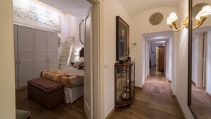 Quarto com cama, cômoda, espelho e corredor que dá para outro ambiente.