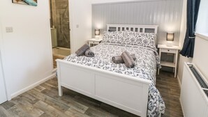 Quarto com cama, mesas de cabeceira, um armário para objetos pessoais, uma pintura e zona de chuveiro.