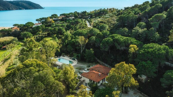 Uma vila com piscina, rodeada por floresta densa e com vista para a costa.