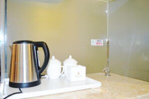 Quarto de hotel com uma chaleira metálica, bules brancos e uma pequena caixa em forma da Torre Eiffel em uma bancada de mármore.