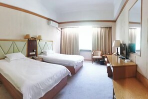 Quarto de hotel com duas camas, uma escrivaninha, uma cadeira e uma televisão.
