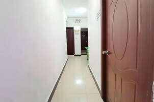 Um corredor com uma porta à direita, uma cadeira verde e uma placa na parede.