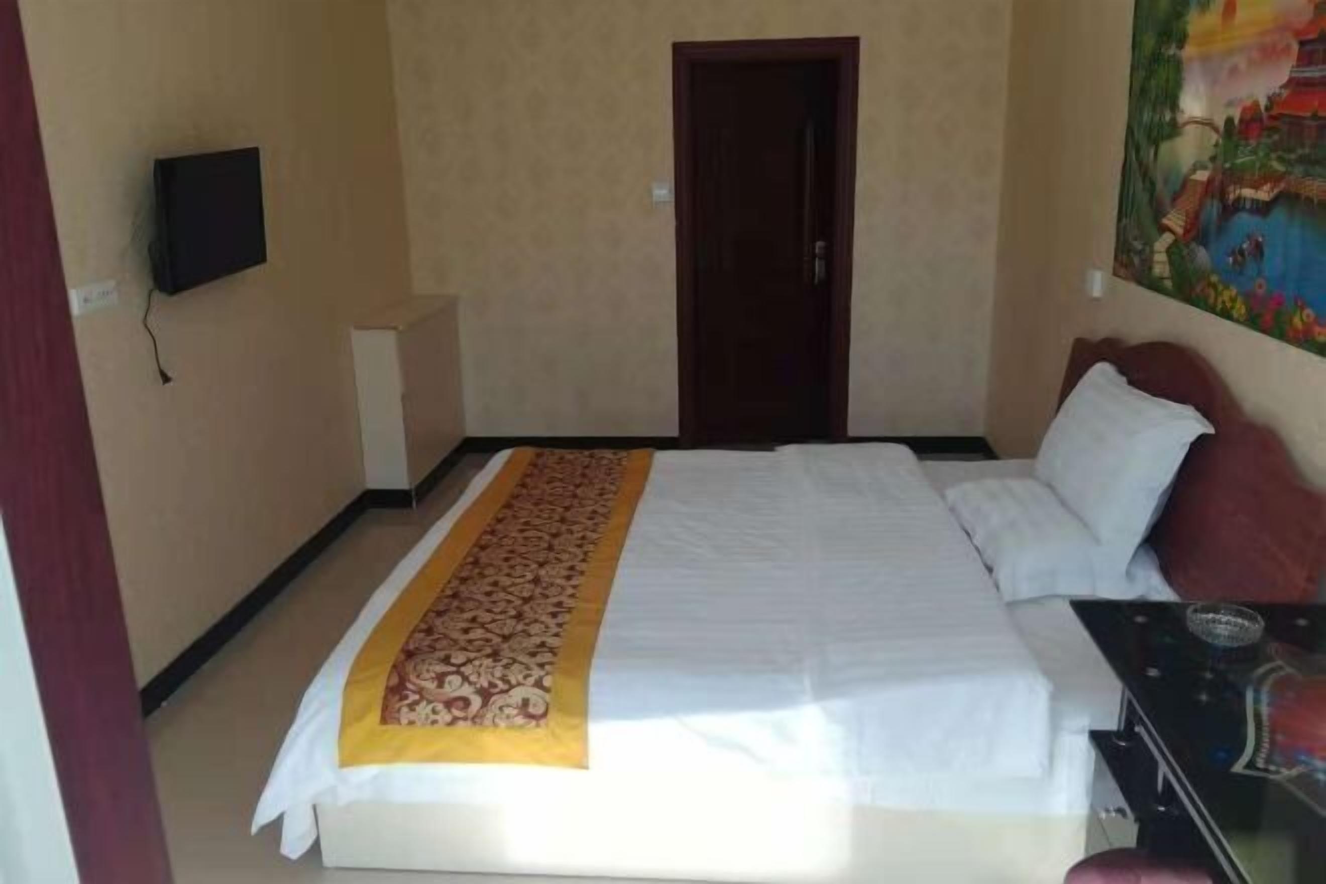 Quarto de hotel com cama, porta, televisão presa na parede e um quadro.