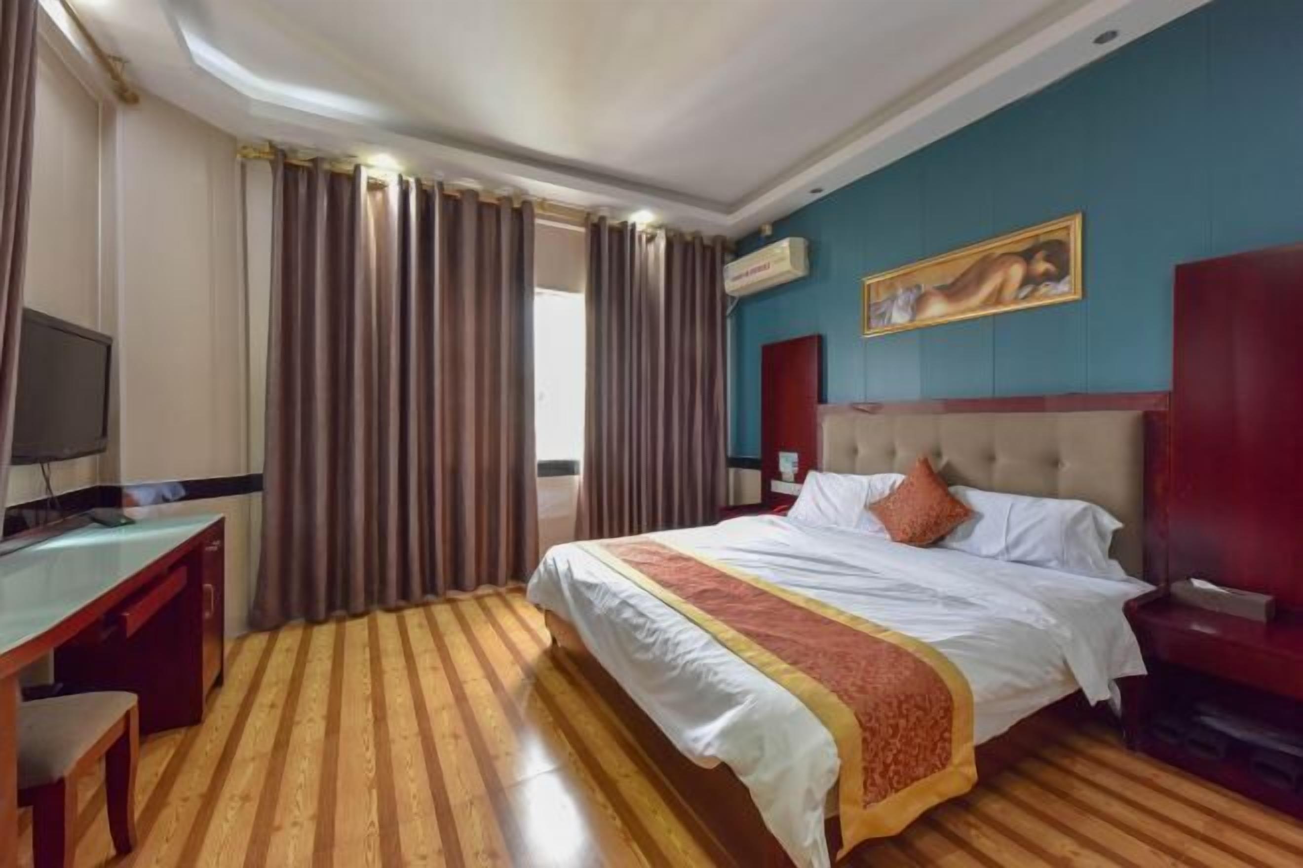 Quarto de hotel com cama, escrivaninha, televisão e um quadro na parede.