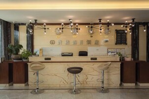 Um balcão de recepção com bancada de mármore, dois bancos altos e uma luminária fixada na parede.