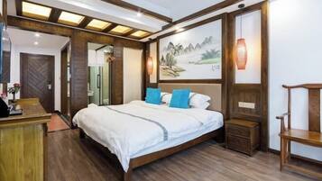 Quarto de hotel com uma cama grande, cabeceira de madeira, uma escrivaninha e uma mesa de cabeceira.