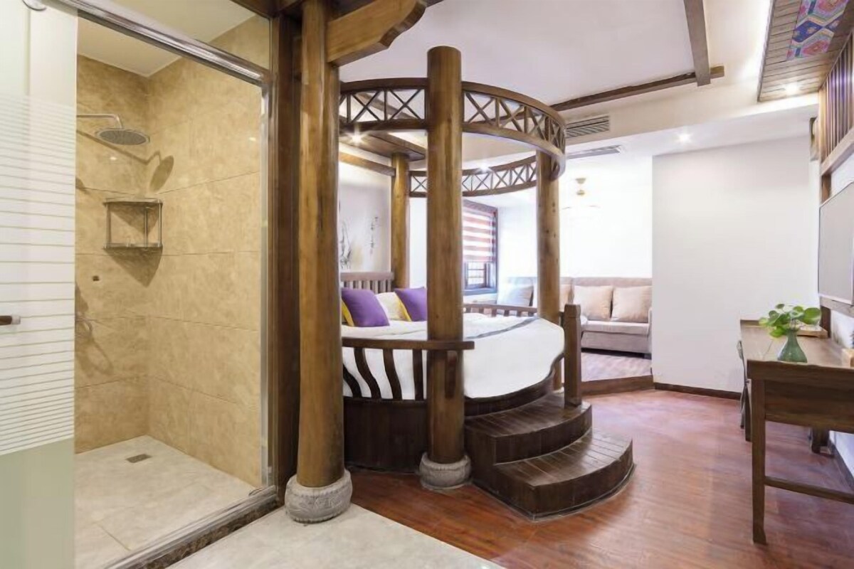 Quarto com estrutura circular de madeira, cama com roupa de cama listrada e uma pequena mesa com uma planta.