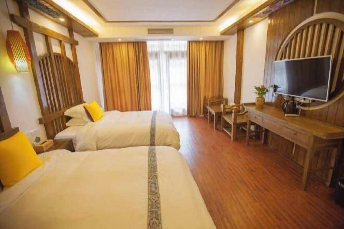 Quarto de hotel com duas camas, uma escrivaninha, uma cadeira e uma televisão.