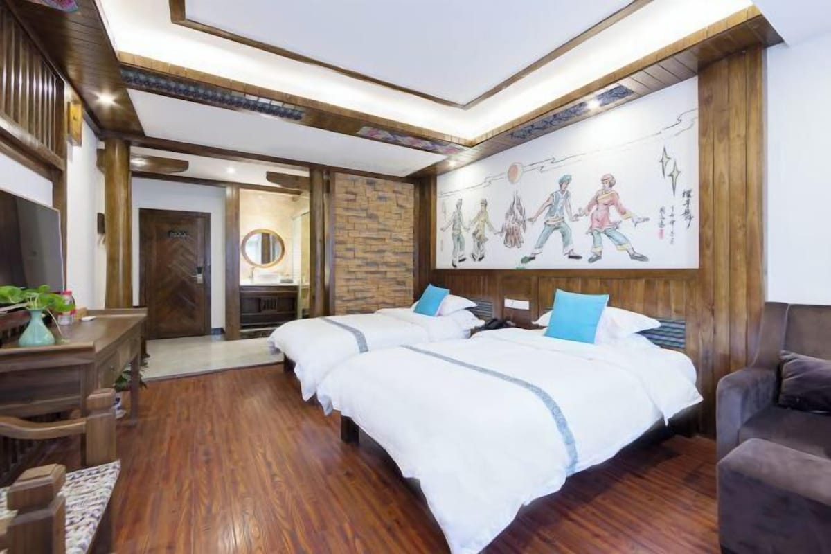 Quarto com duas camas, piso de madeira, parede de destaque em pedra e um mural na parede.