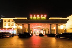 Entrada de hotel com uma placa grande, área de acesso coberta e vários carros estacionados na frente.