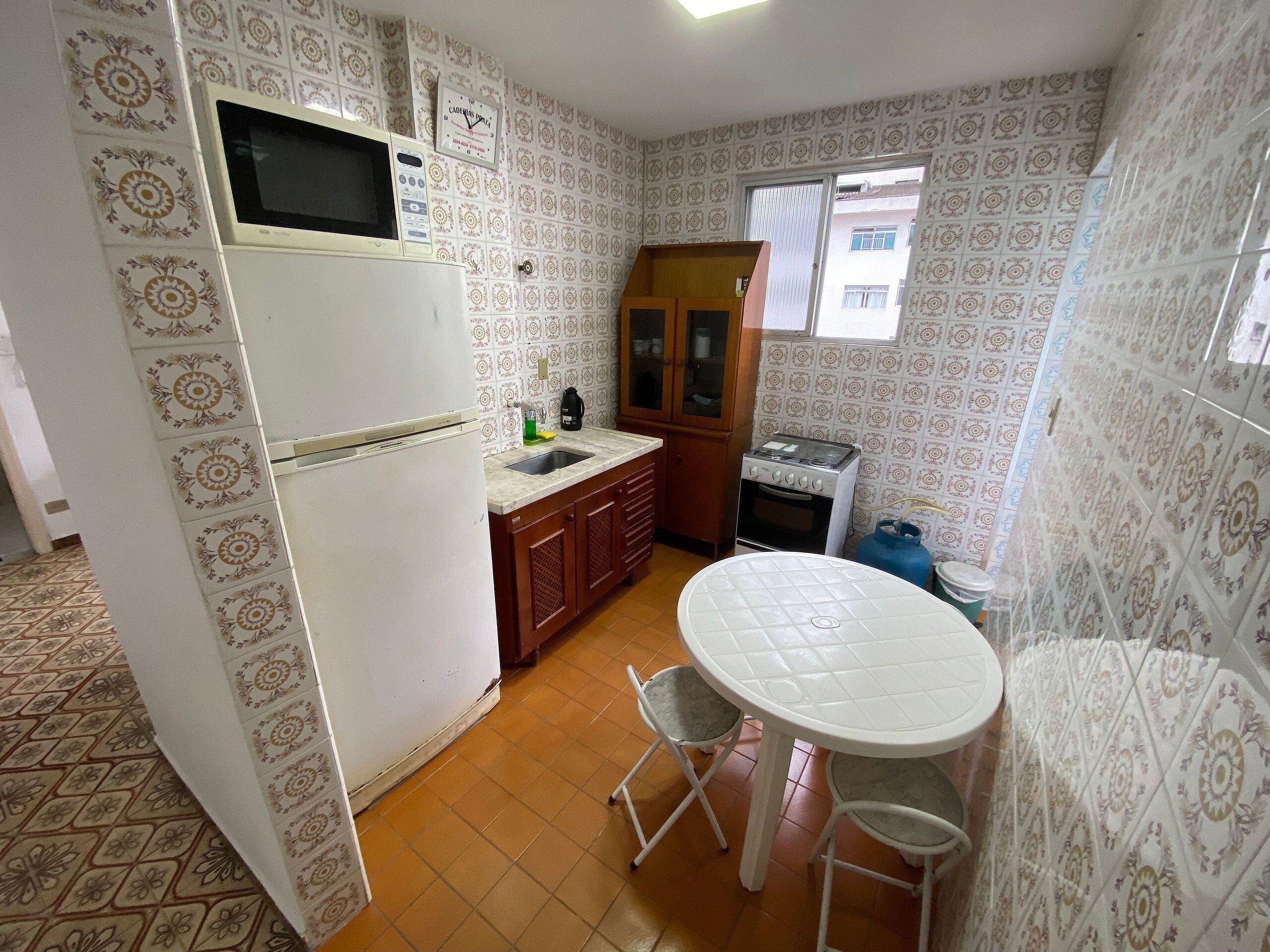 Cozinha compacta com geladeira, micro-ondas, pia, fogão e uma pequena mesa de jantar com cadeiras.