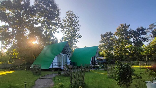 Um edifício moderno com telhado verde e fachada de vidro, rodeado por um jardim bem cuidado e árvores.