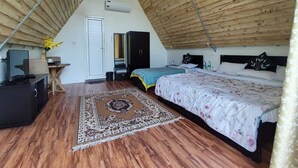 Quarto com teto inclinado, cama com roupa de cama floral, uma pequena escrivaninha e uma cadeira.