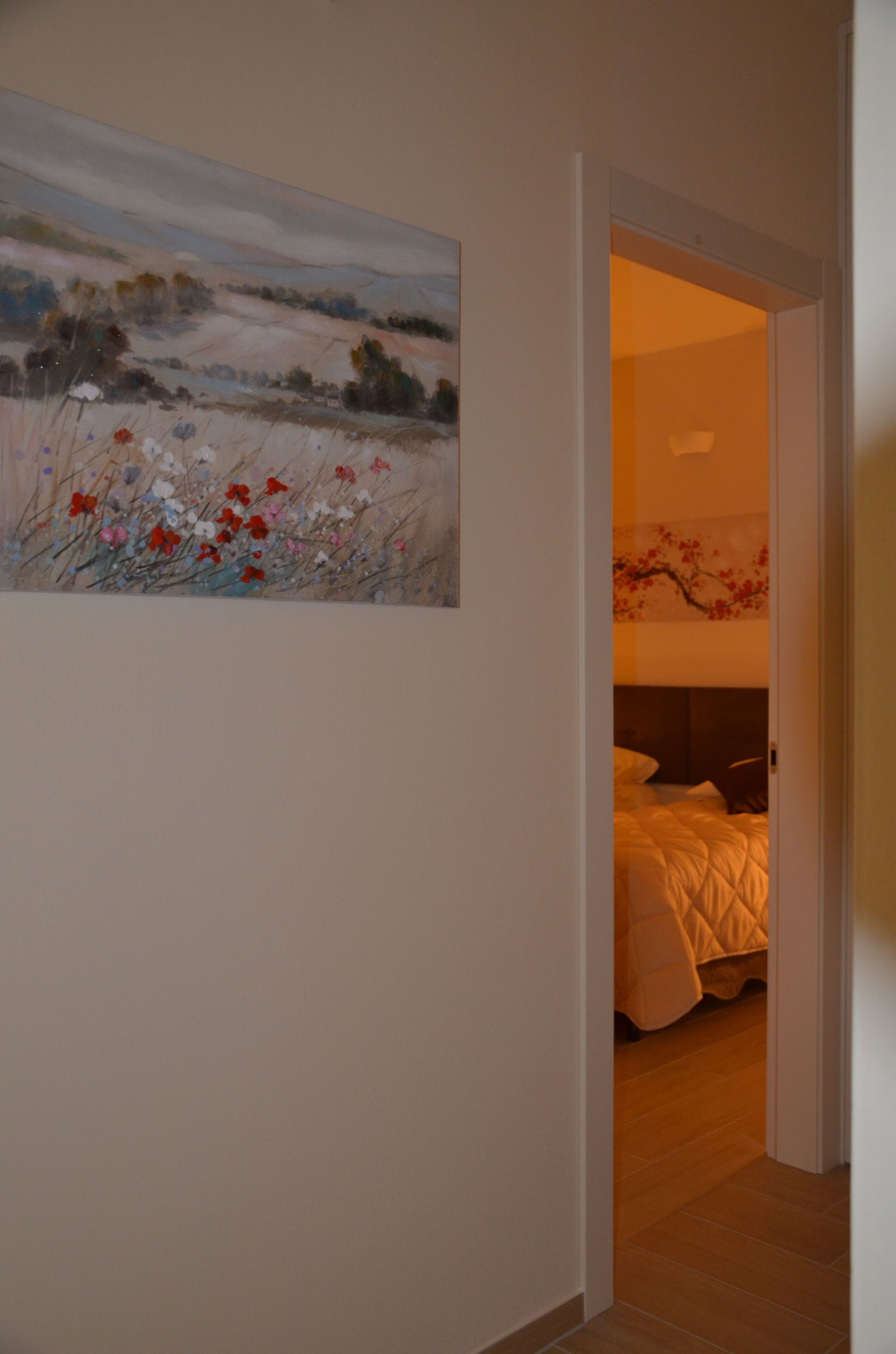 Quarto com uma cama, um quadro na parede e vista para outro cômodo.