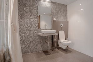 Um banheiro moderno com parede em mosaico de azulejos, pia independente, vaso sanitário e área de chuveiro.