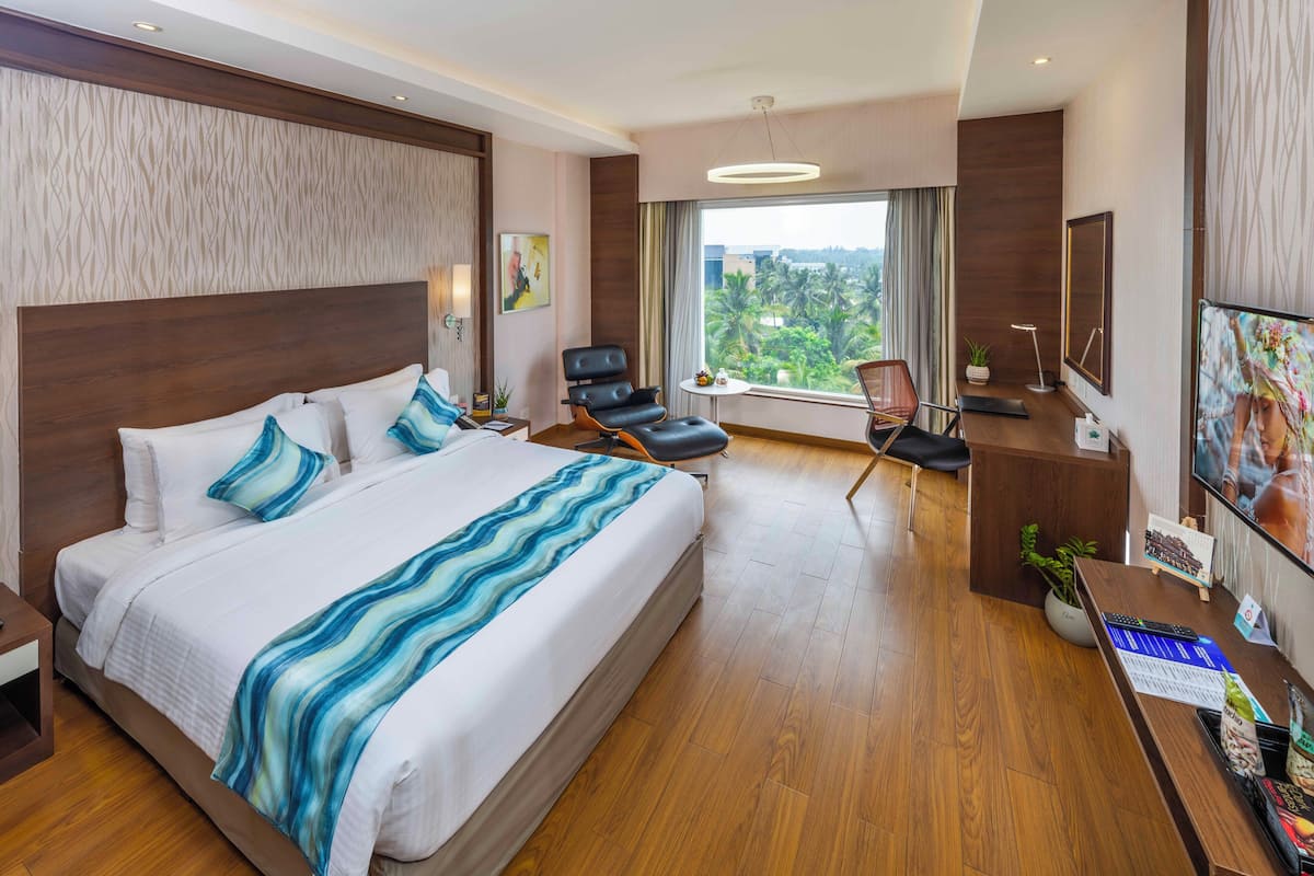 Quarto de hotel com uma cama grande, uma mesa, uma cadeira, uma TV e uma janela com vista para a cidade.