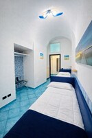 Um quarto com cama, uma cadeira, uma mesinha, um ventilador de teto e um quadro na parede.
