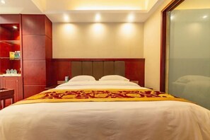 Quarto de hotel com uma cama grande, cabeceira de madeira, mesa de cabeceira e guarda-roupa.