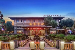 Um hotel com estilo arquitetônico tradicional, destacando uma entrada imponente com placa, área de estar ao ar livre e paisagismo bem cuidado.