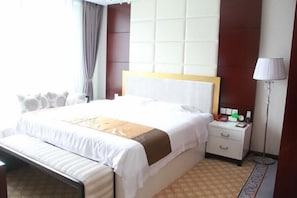 Quarto de hotel com cama, mesa de cabeceira, abajur e piso estampado.