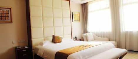 Quarto de hotel com cama grande, mesa de cabeceira, cadeira e janela com cortinas.