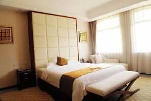 Quarto de hotel com cama grande, mesa de cabeceira, cadeira e janela com cortinas.