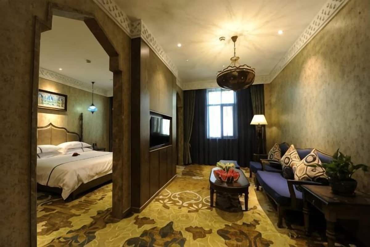 Quarto de hotel com cama, sofá, televisão e uma mesa de jantar.