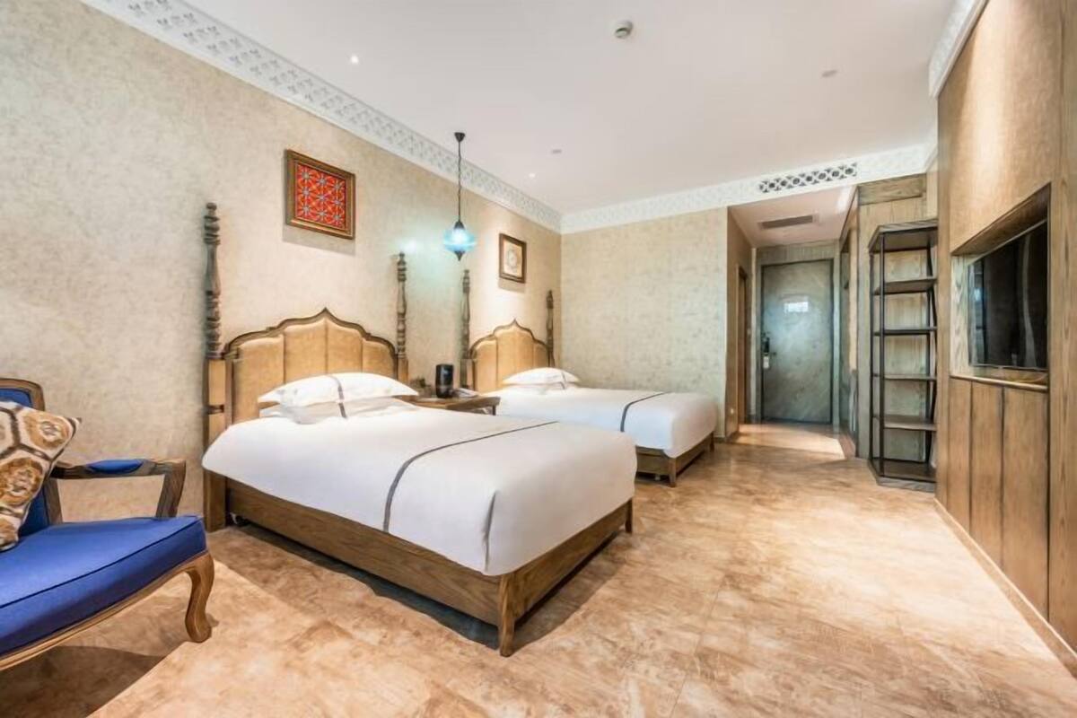 Quarto de hotel com duas camas, uma cadeira azul e um guarda-roupa de madeira.