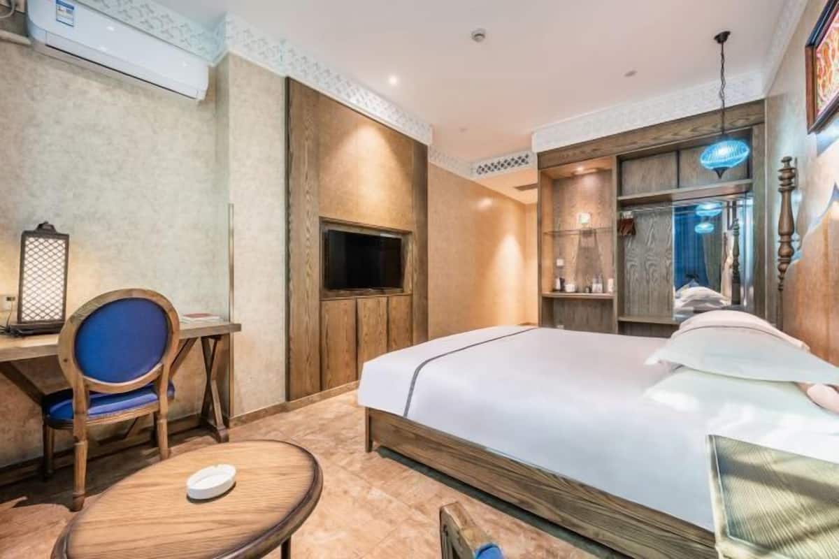 Quarto de hotel com cama, escrivaninha, cadeira, televisão e guarda-roupa.