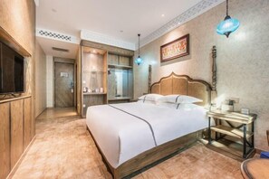 Quarto de hotel com uma cama grande, uma mesa de cabeceira de madeira, televisão presa à parede e luminária no teto.