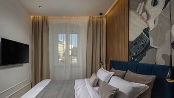 Quarto de hotel com cama, televisão, janela grande com cortinas e um mural na parede.