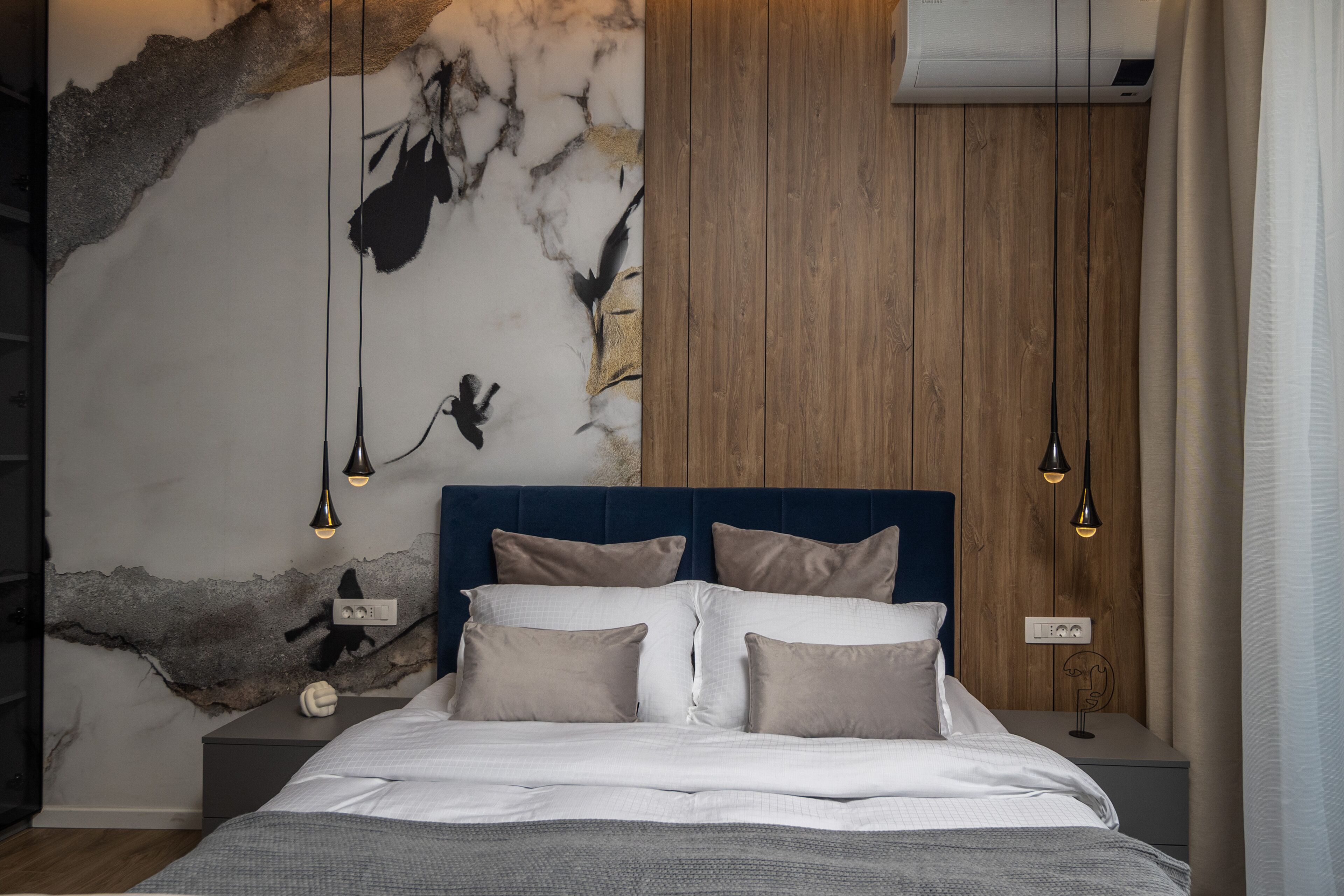 Quarto com cama, painel de madeira, parede de mármore e luminárias pendentes.