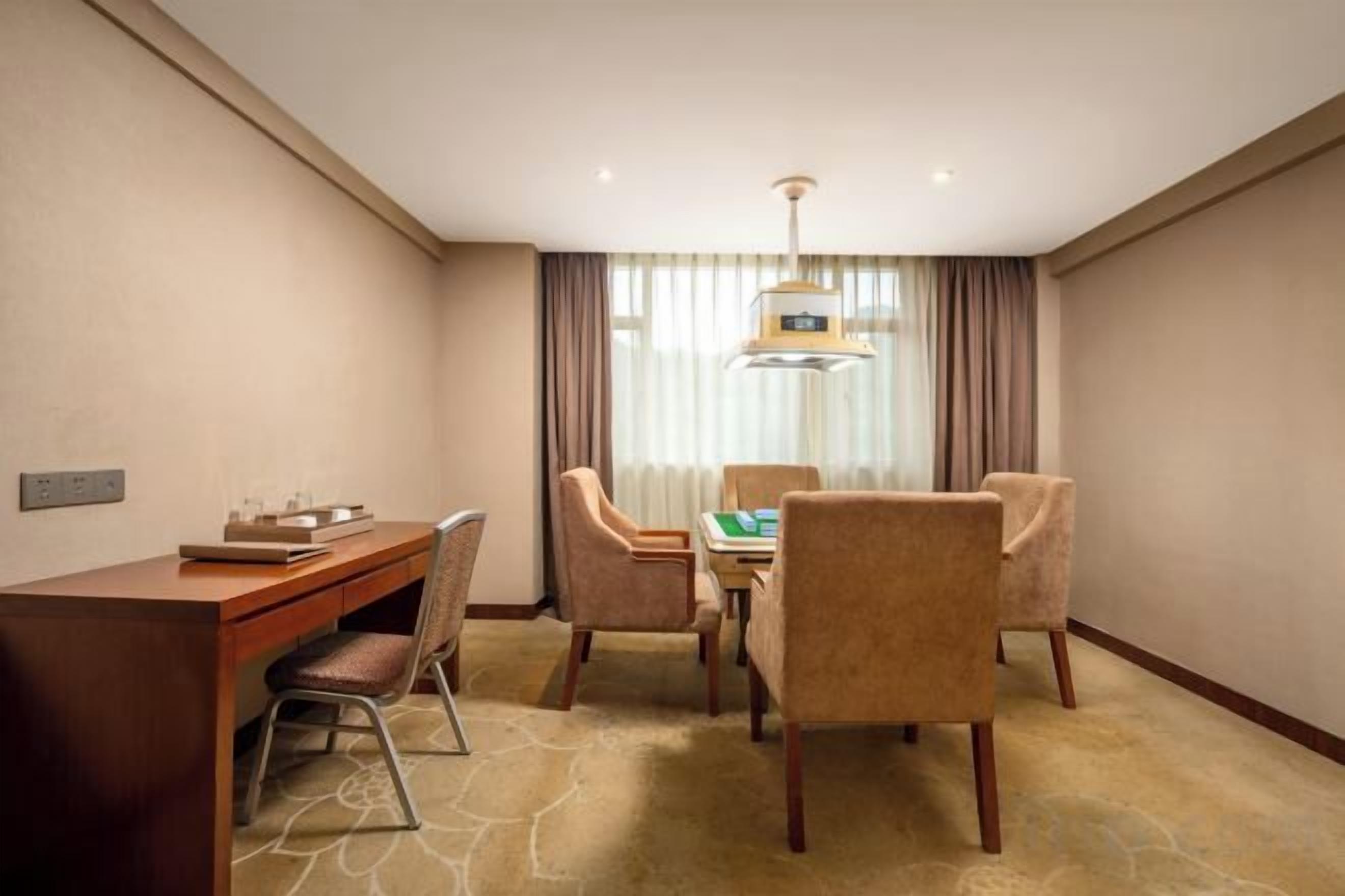 Quarto de hotel com uma mesa de jantar, quatro cadeiras, uma escrivaninha e um candelabro.