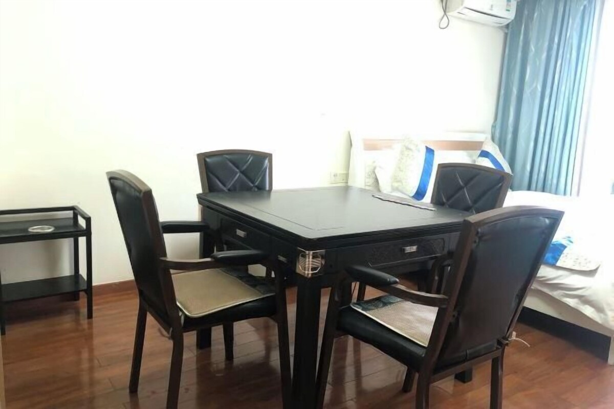 Um quarto pequeno e bem arrumado com uma mesa de madeira escura e quatro cadeiras, uma mesinha de apoio e uma cama com cortina azul.
