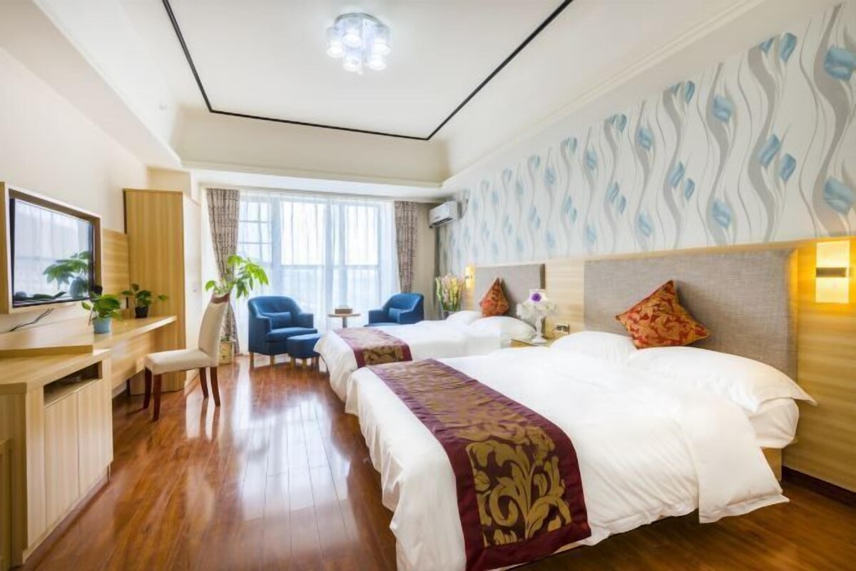 Quarto de hotel com duas camas, uma escrivaninha, uma cadeira e uma televisão.