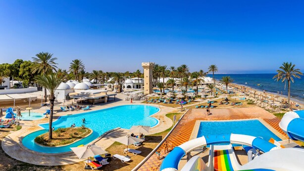 Um resort com uma piscina grande, toboáguas, praia e palmeiras.