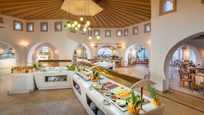 Uma área de buffet com diversas opções de comida, um ponto central de serviço e um espaço de refeições com mesas e cadeiras.